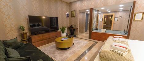 Quarto de hotel com televisão, sofá, puf, cama e espelho de banheiro.