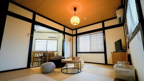 Um quarto japonês tradicional com tatames, uma mesa redonda e um candeeiro suspenso.