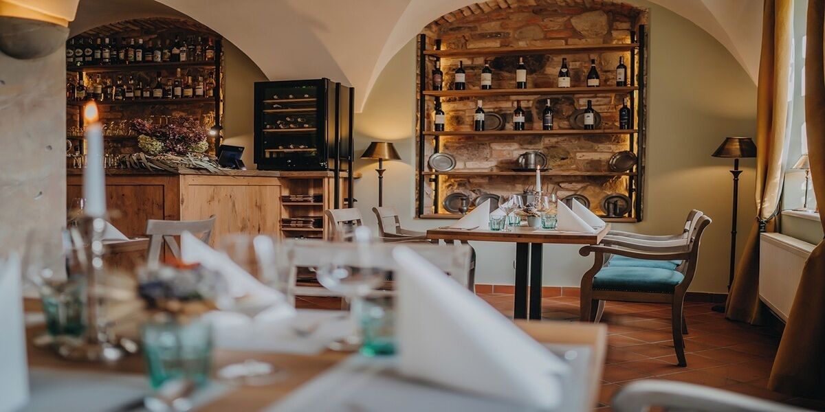 Um restaurante com parede de pedra rústica, prateleiras de madeira com garrafas e uma mesa posta para refeição.