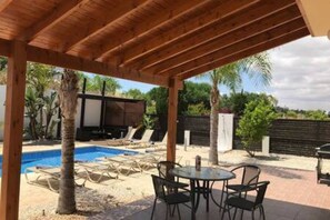 Um pátio externo com piscina, espreguiçadeiras e uma mesa.