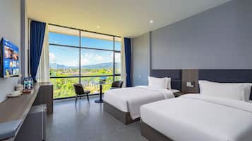 Quarto de hotel com duas camas, uma escrivaninha com computador, uma mesinha pequena e uma janela grande com vista para o exterior.