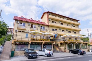 Um hotel com vários andares, varandas, área de estar externa e uma escadaria que leva à entrada.