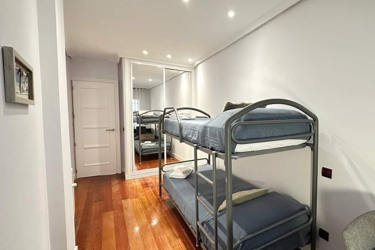 Quarto com beliches, piso de madeira, porta e espelho.