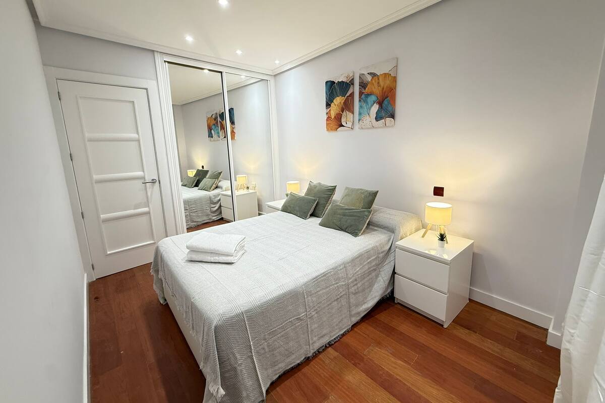 Quarto com cama, mesas de cabeceira, espelho e obras de arte na parede.