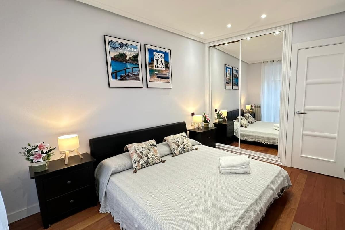 Quarto com cama, mesas de cabeceira, espelho e quadros na parede.