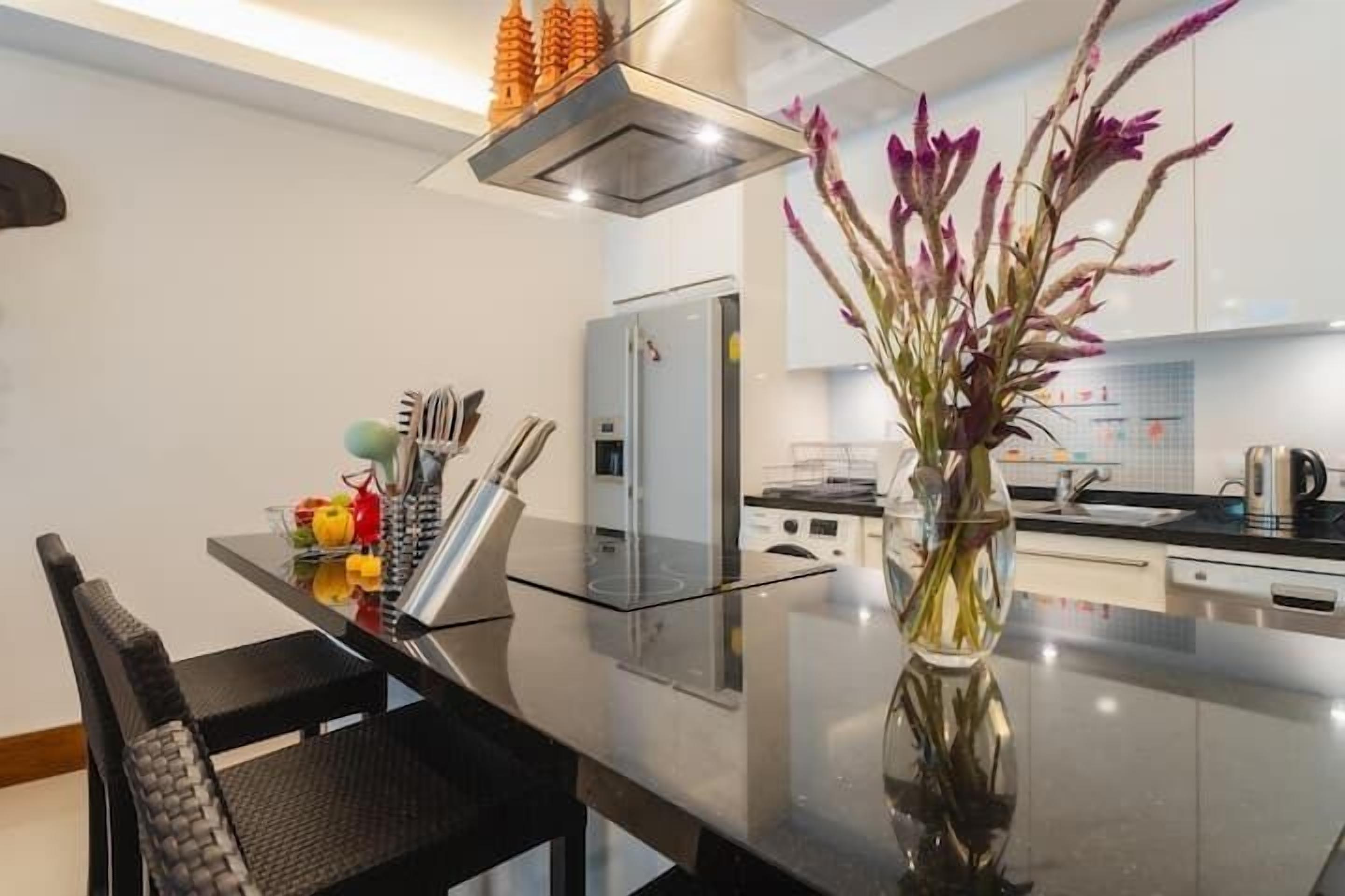 Uma cozinha moderna com mesa de jantar de vidro, eletrodomésticos de aço inoxidável e um vaso com flores.