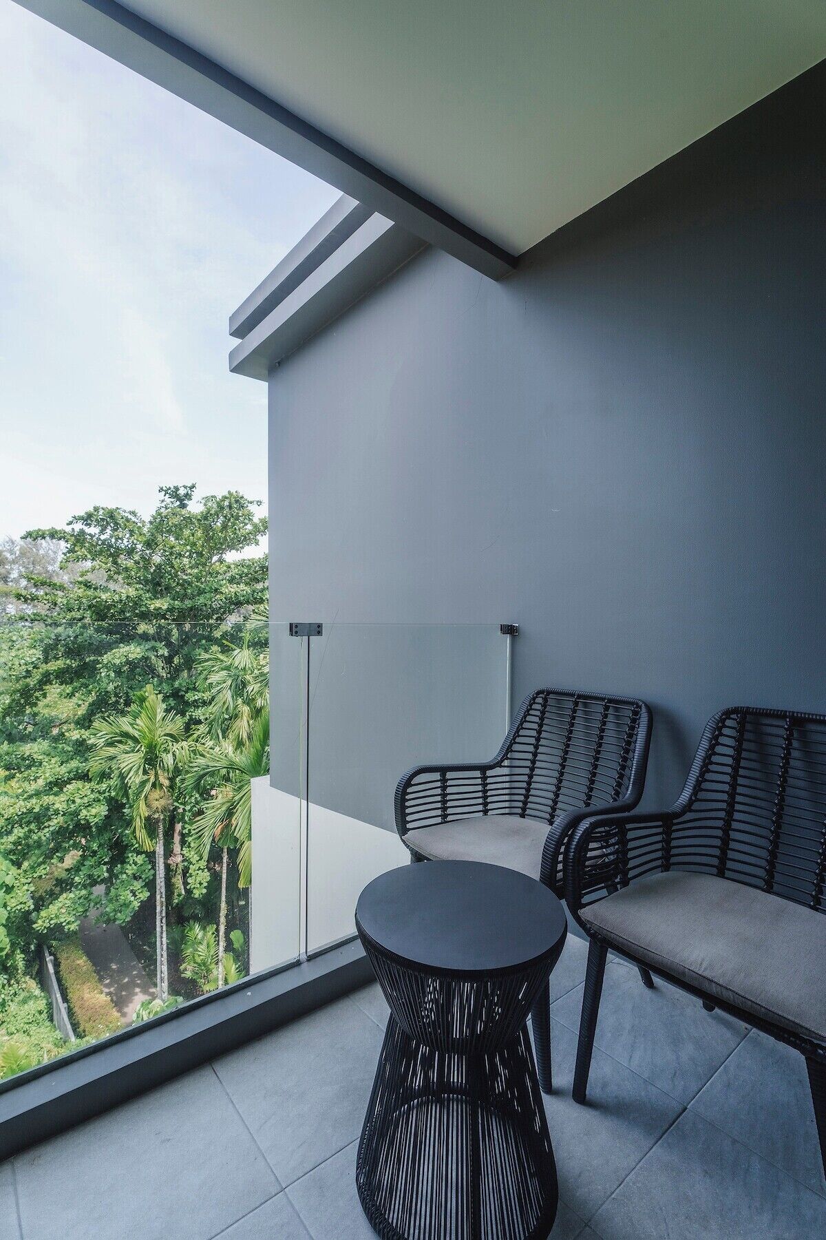 Varanda com design moderno, com duas cadeiras de vime preto e uma mesa redonda pequena.