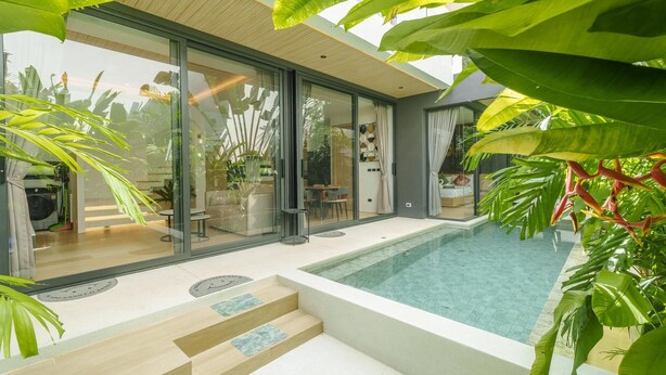Uma casa moderna com fachada de vidro, piscina e vegetação tropical exuberante.