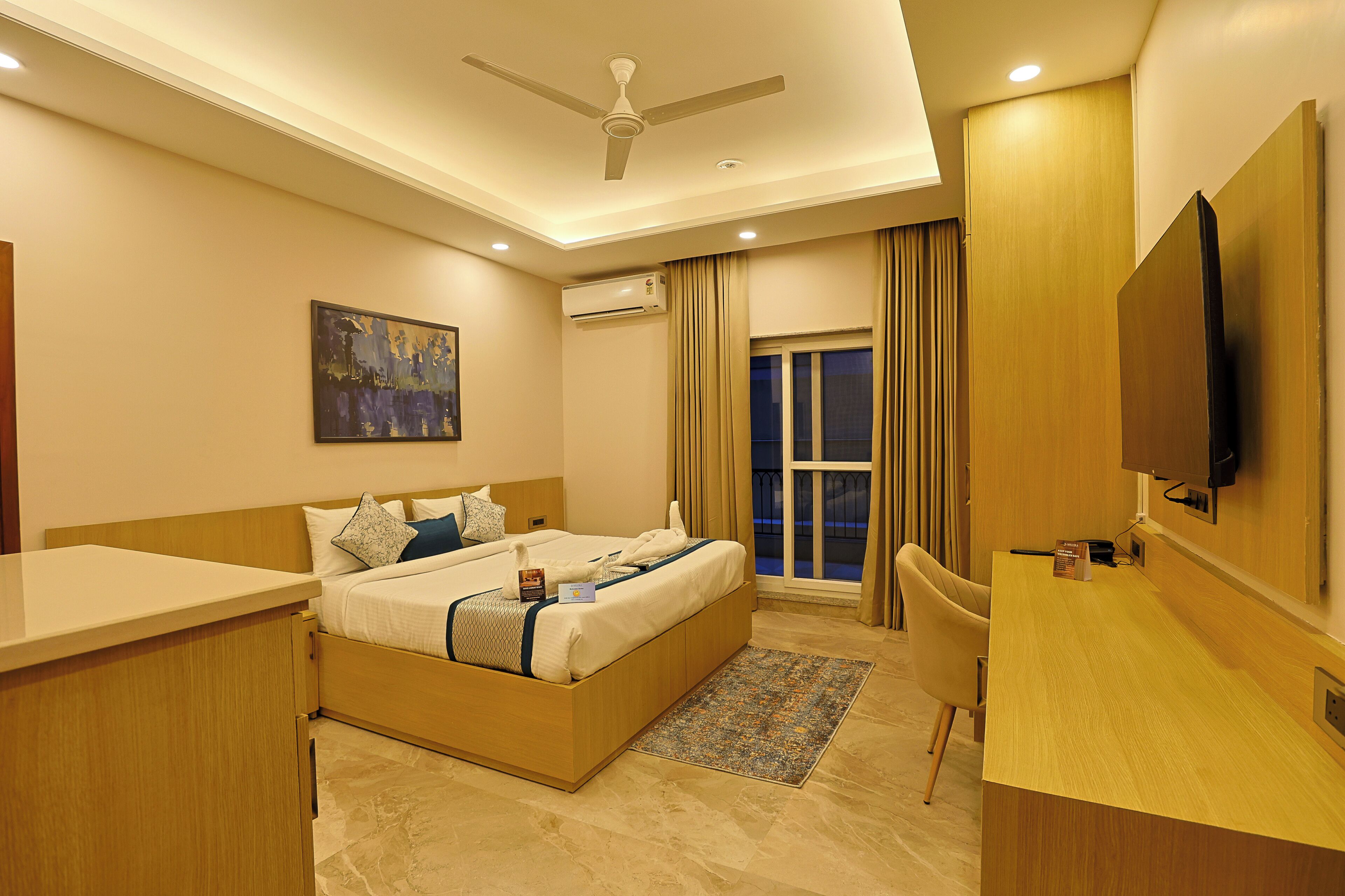 Quarto de hotel moderno com cama, escrivaninha, cadeira, televisão, ar condicionado e vista para o exterior.