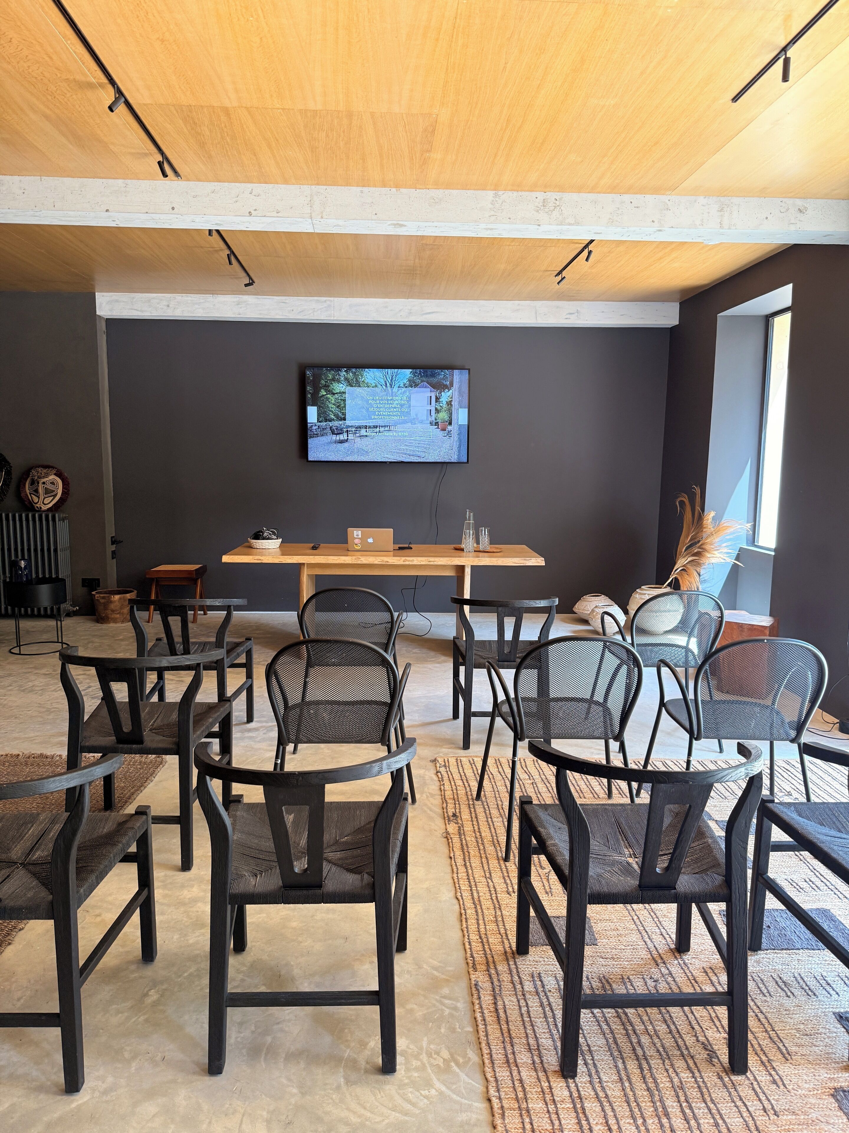 Uma sala de reunião moderna com uma mesa grande, cadeiras de malha preta e uma televisão na parede.