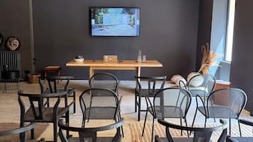 Uma sala de reunião moderna com uma mesa grande, cadeiras de malha preta e uma televisão na parede.