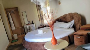 Quarto com cama, mesa de cabeceira e uma pequena mesa com um vaso.