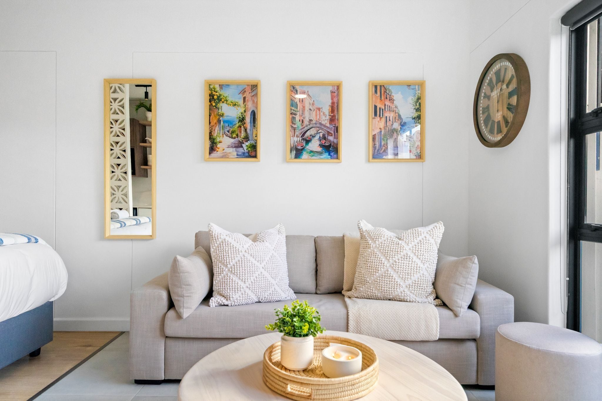 Uma sala de estar moderna com um sofá, almofadas decorativas, uma mesa de centro com uma planta e velas, e três quadros na parede.