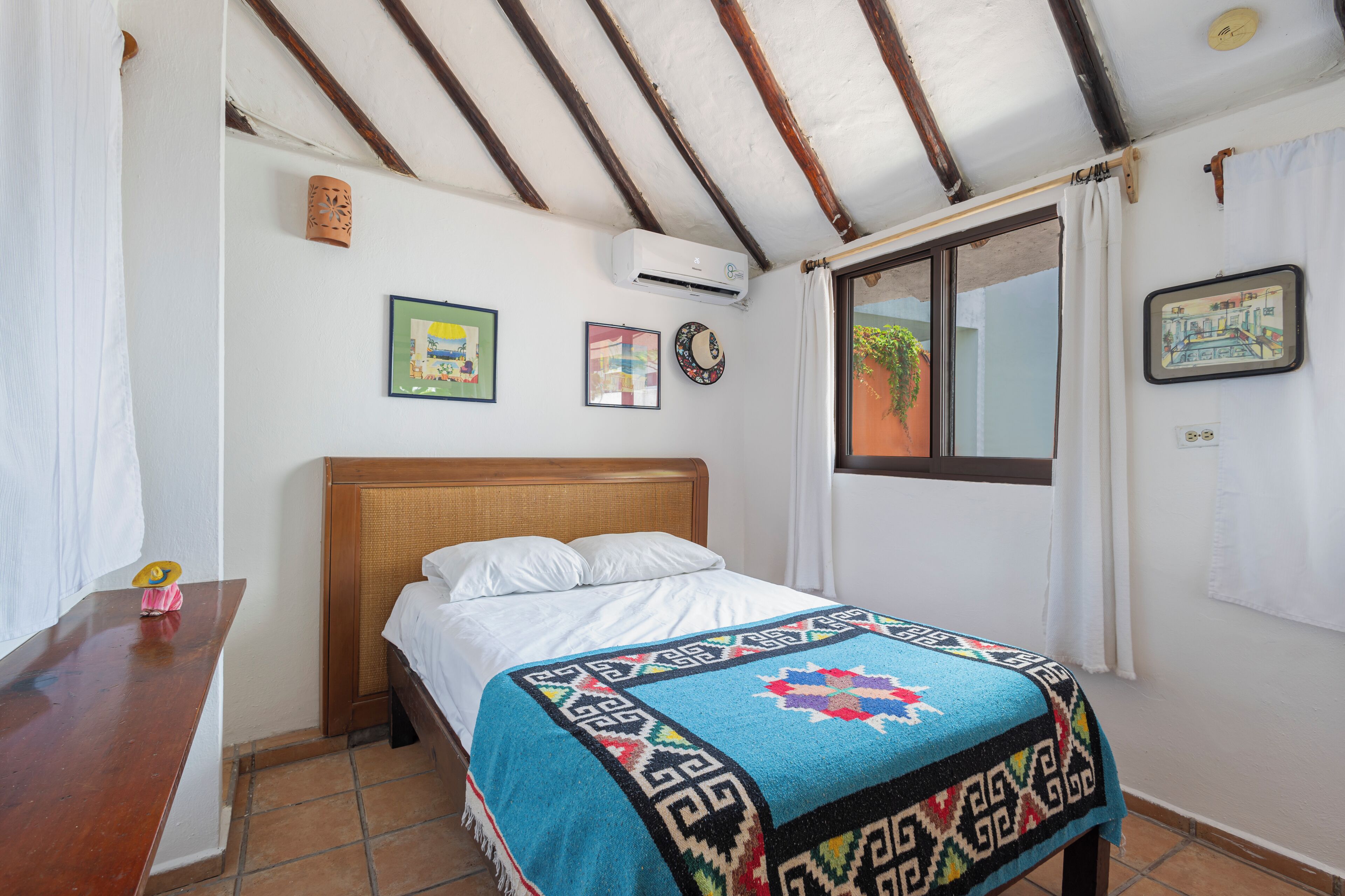 Quarto com cama de madeira, janela com cortinas e ar-condicionado fixado na parede.