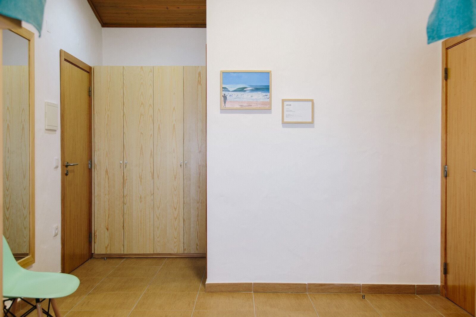 Um corredor com portas de madeira, um quadro na parede e uma cadeira no canto.