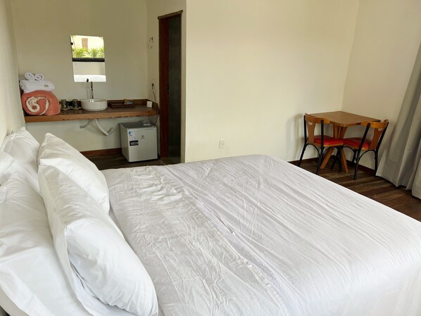 Quarto de hotel com cama, escrivaninha, cadeira, pequeno frigorífico e janela com vista.