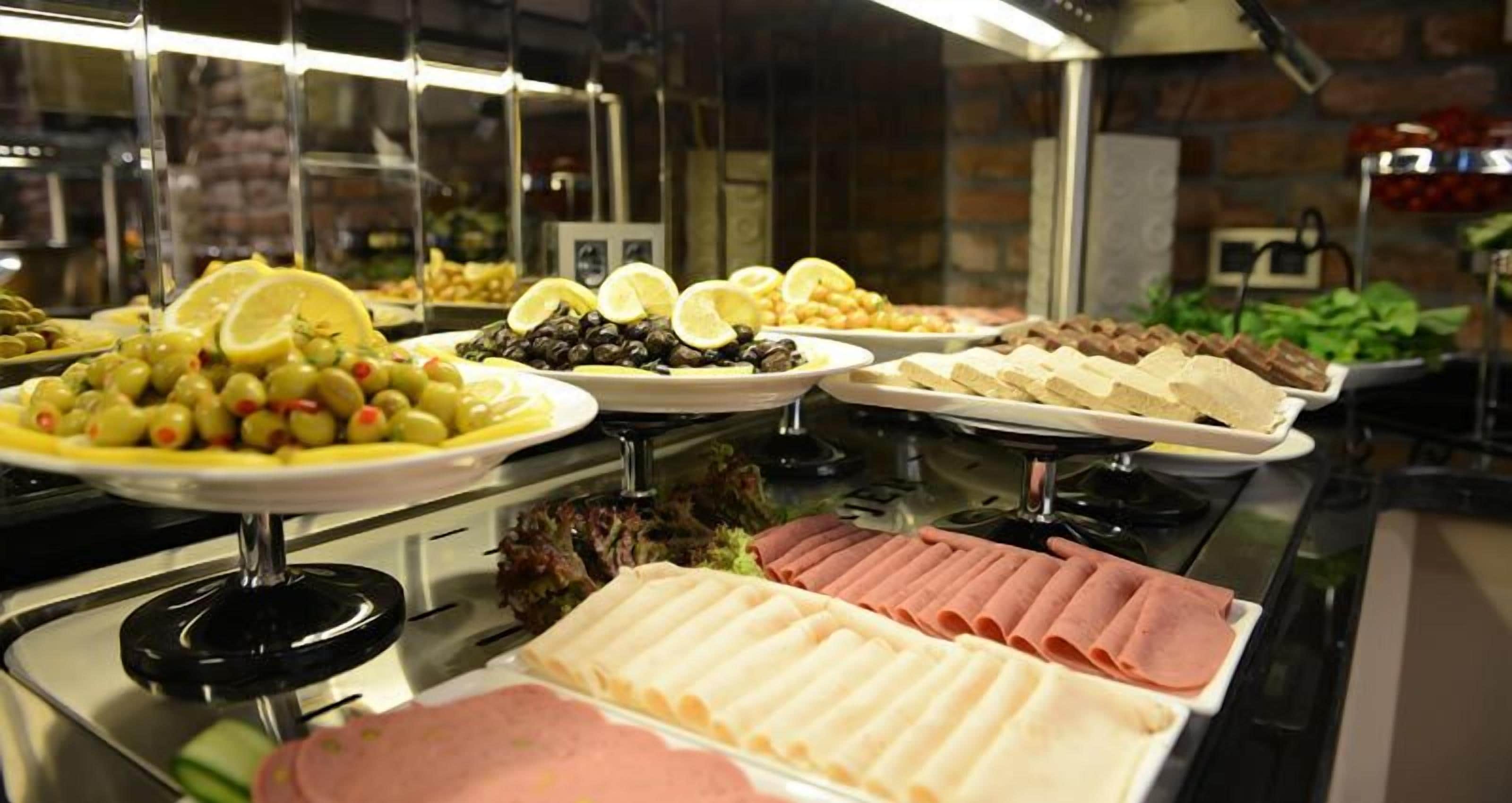 Buffet com diversos alimentos, incluindo azeitonas, queijos e carnes.