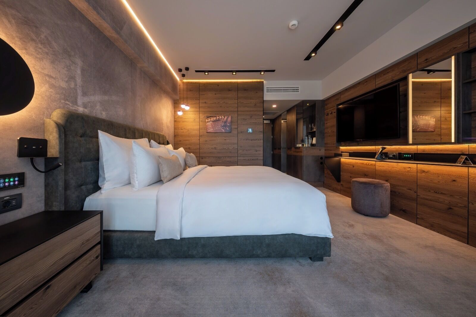 Quarto moderno com uma cama grande, mesa de cabeceira, televisão e painel de parede de madeira.