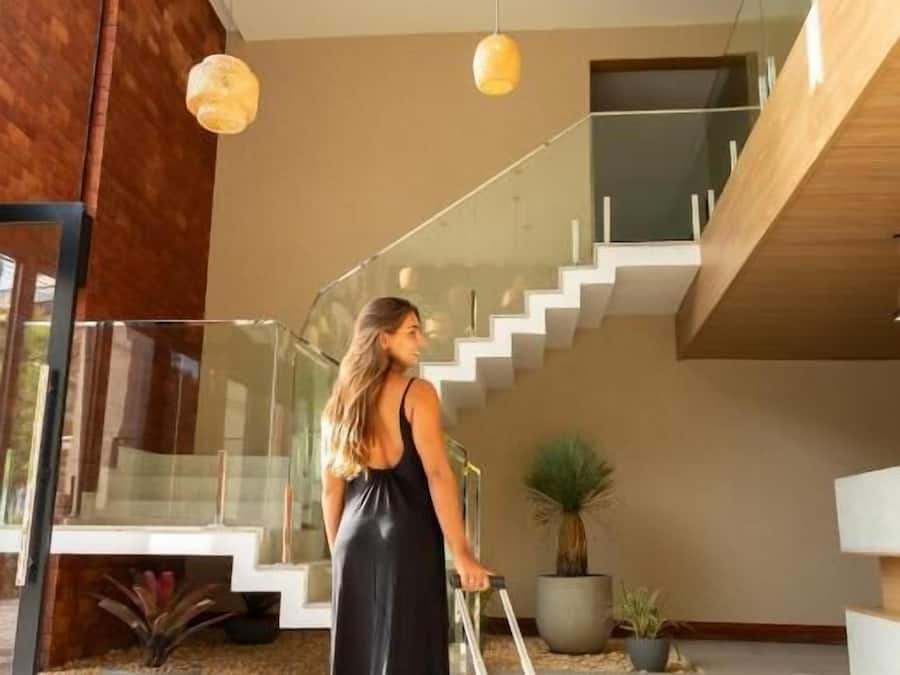 Interior moderno com escada, uma mulher com mala e luminárias pendentes.