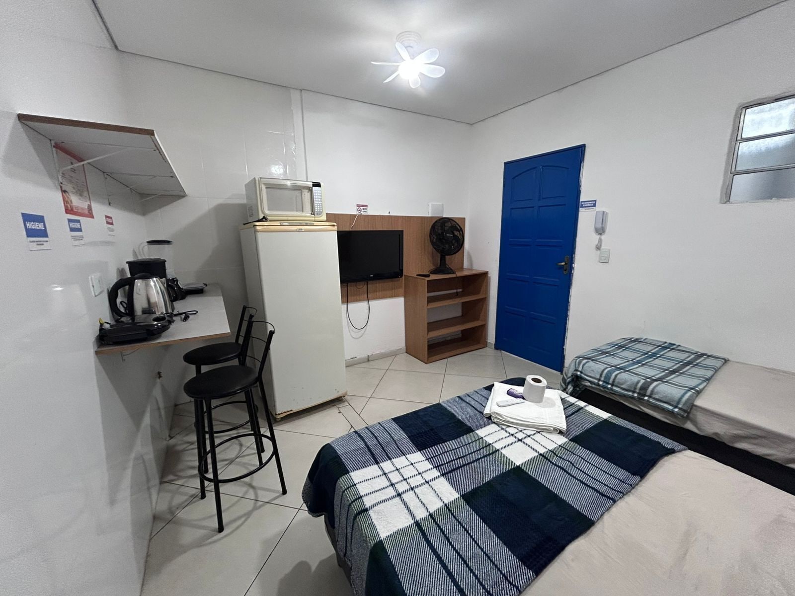 Quarto compacto com cozinha compacta, uma cama de solteiro, uma cadeira e uma porta azul.