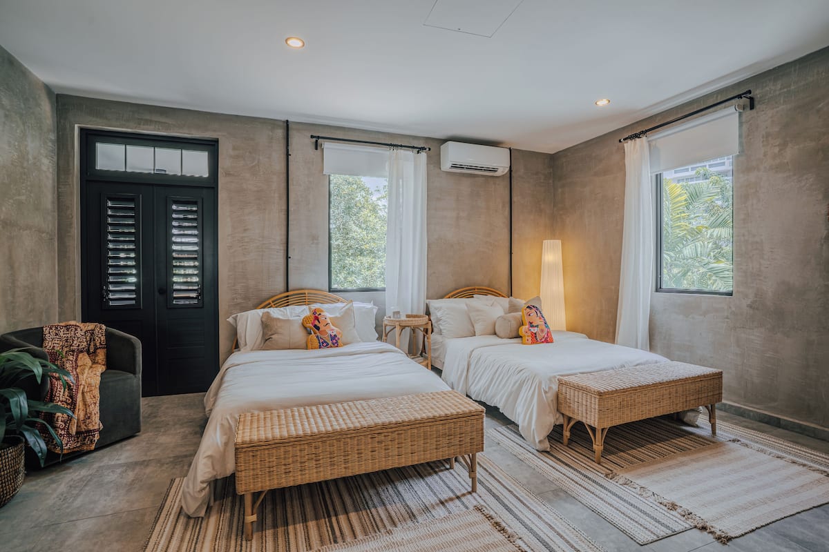 Quarto moderno com duas camas, uma porta escura e janelas grandes.