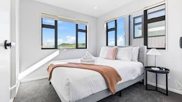 Quarto moderno com uma cama grande, uma mesinha de cabeceira e vista para o exterior através de duas janelas.