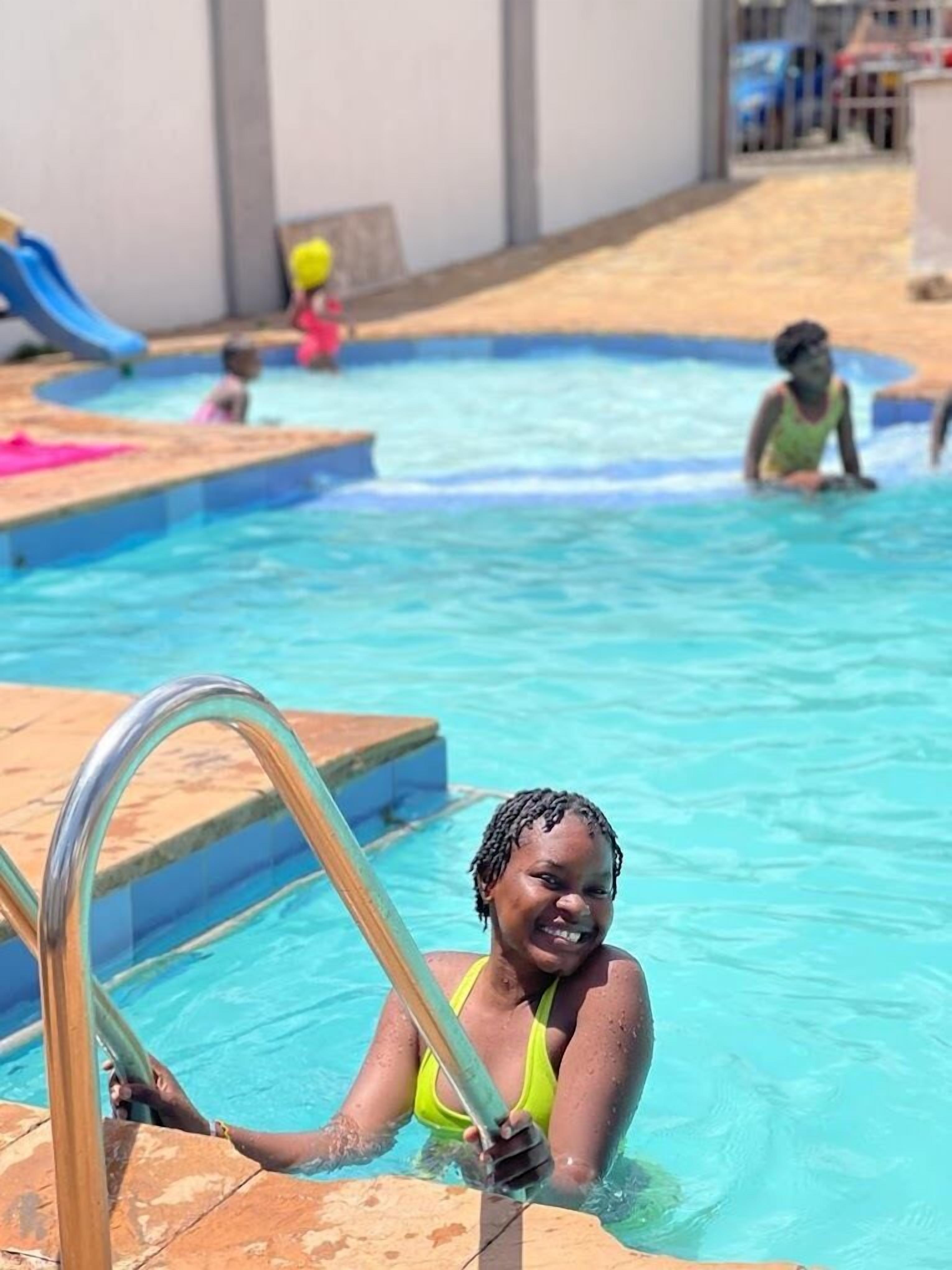 Piscina com um recurso de água cristalina, uma escada de metal e um escorrega ao fundo.