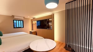 Quarto de hotel moderno com cama, mesa redonda pequena, televisão e janela.