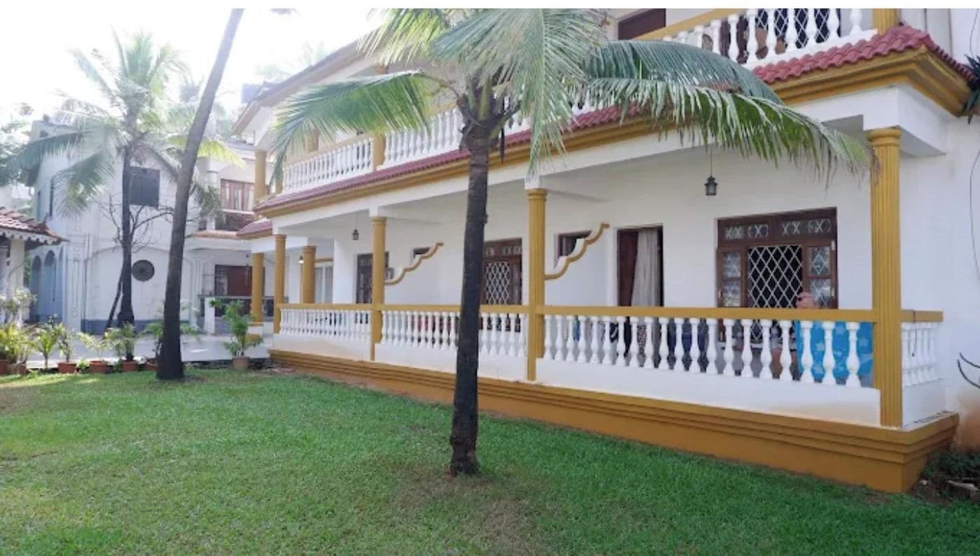 Uma casa de dois andares com varanda, um pequeno jardim e palmeiras.