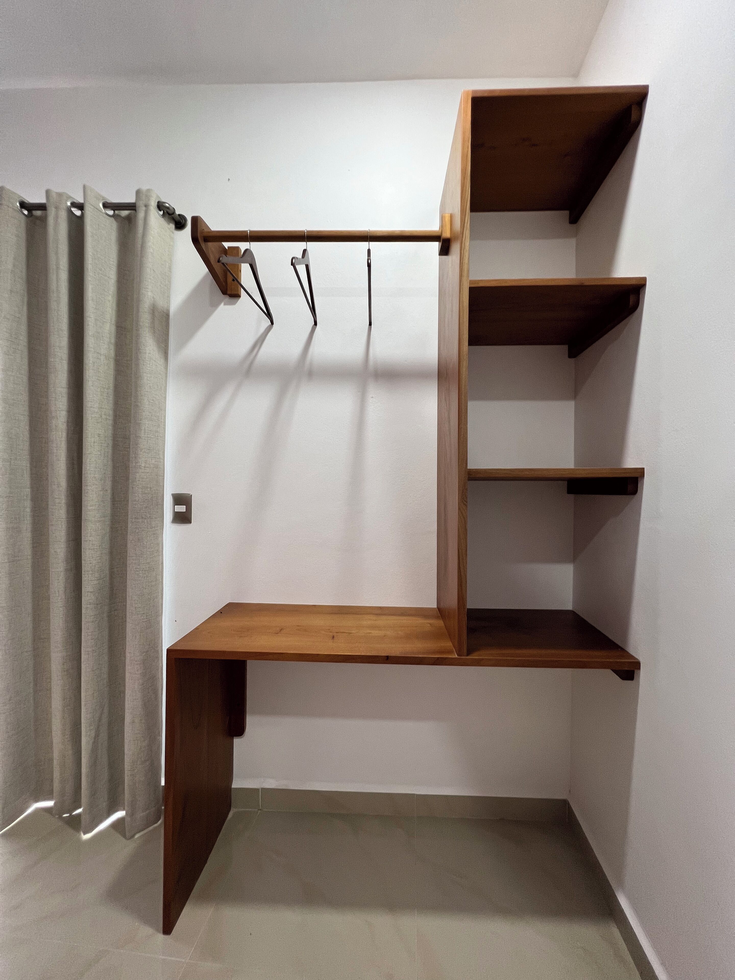 Quarto de canto com escrivaninha de madeira, estantes e porta-casacos.