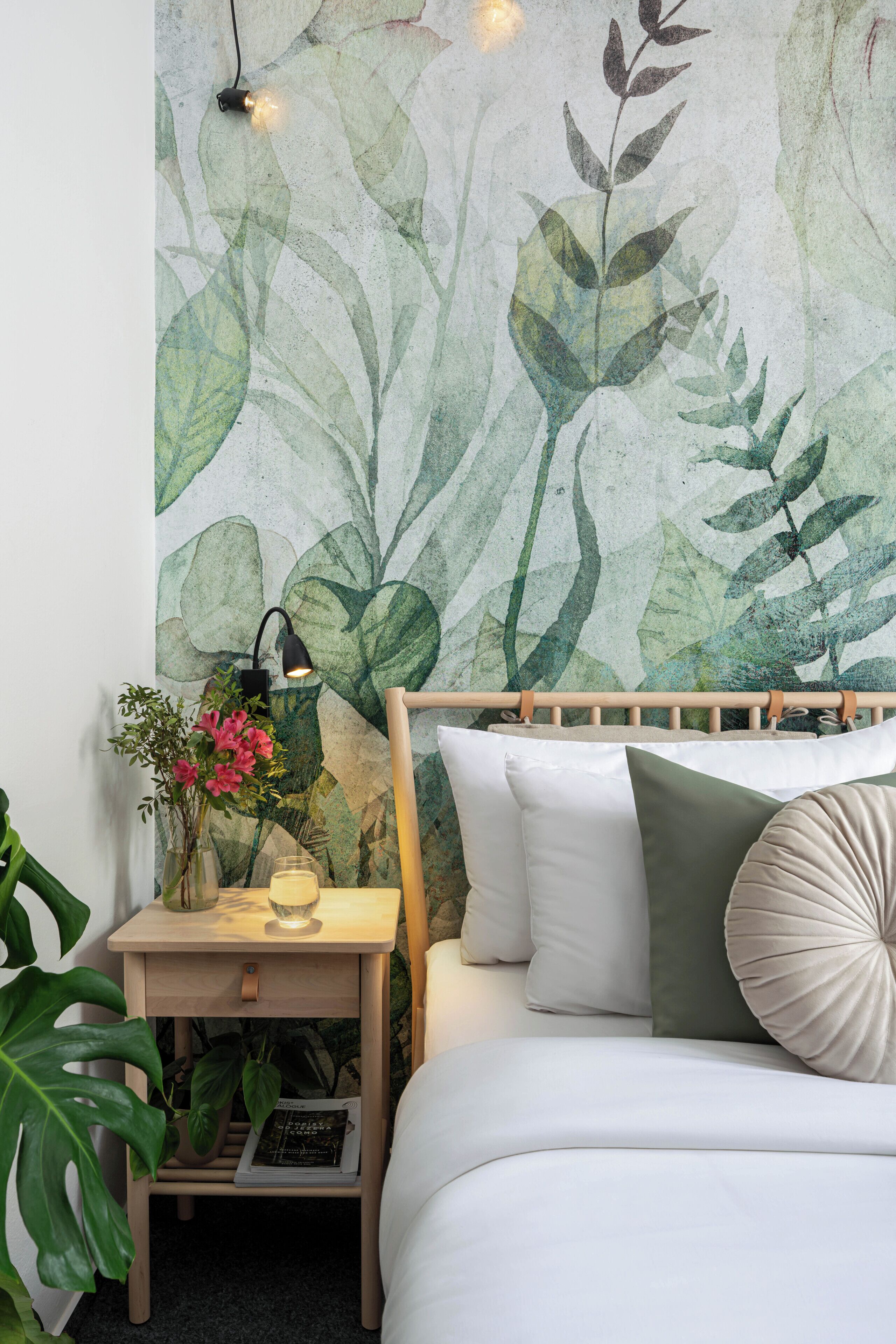 Quarto com cama, mesa de cabeceira, abajur e parede com padrão de folhas.