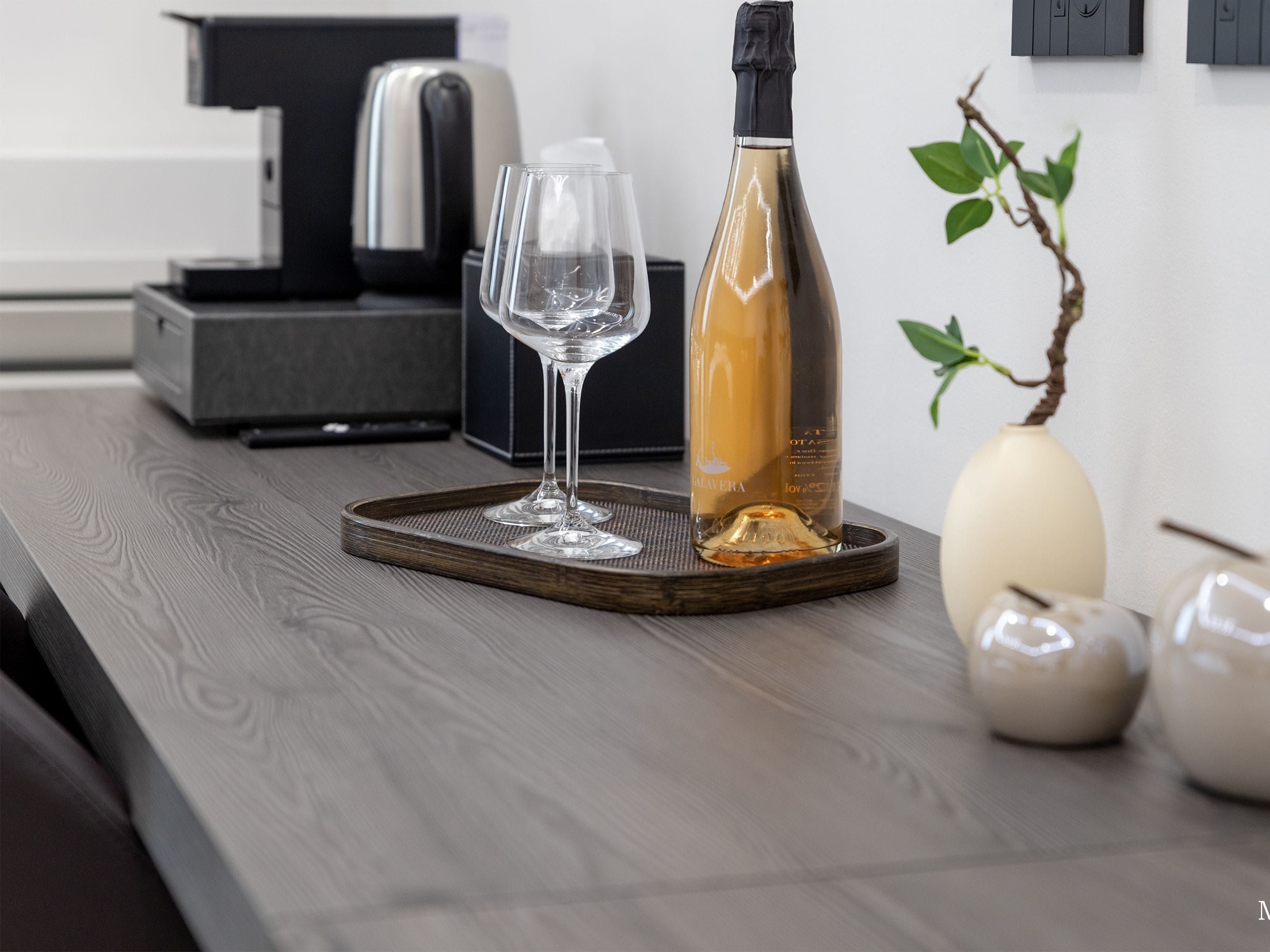 Uma cozinha moderna com bancada de madeira, uma garrafa de vinho, duas taças de vinho, uma máquina de café e um vaso com uma planta.