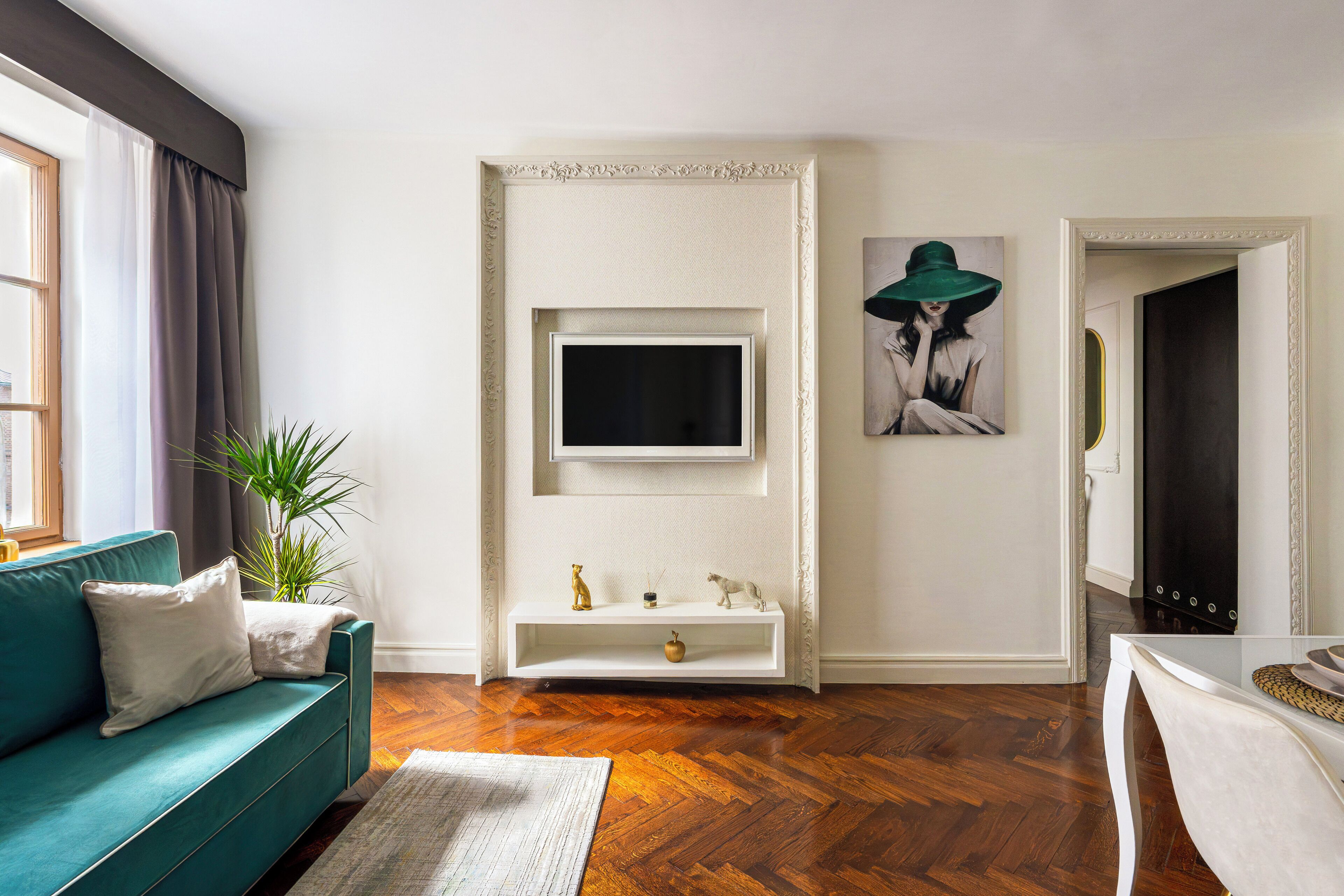 Uma sala de estar com um sofá azul-turquesa, um móvel branco para eletrônicos, uma TV de tela plana, um quadro e piso de madeira.