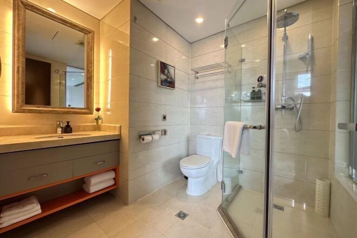 Uma casa de banho moderna com chuveiro envidraçado, um espelho grande e uma toucador com lavatório e porta-toalhas.