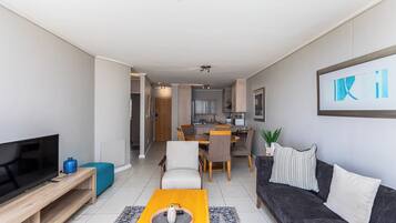 Uma sala de estar moderna com televisão, sofá, mesa de centro e área de jantar.