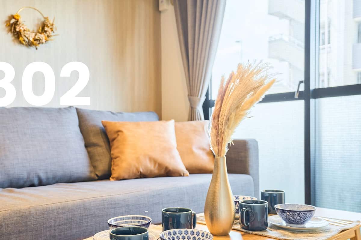 Uma sala de estar moderna com um sofá cinzento, um vaso com plumas de pluma, e uma mesa com tigelas e chávenas.