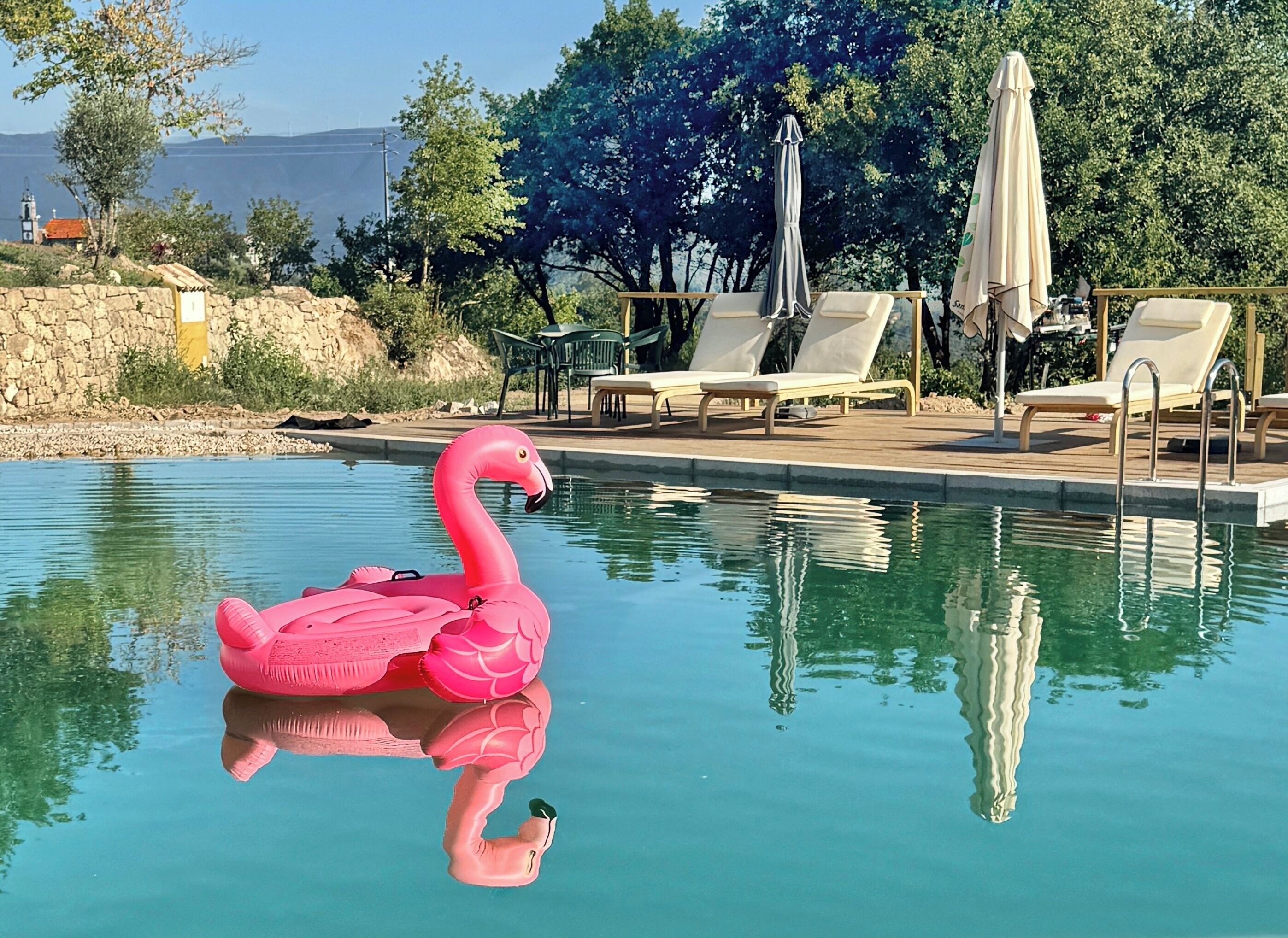 Piscina com um flutuador de flamingo rosa, cadeiras de descanso e um muro de pedra.