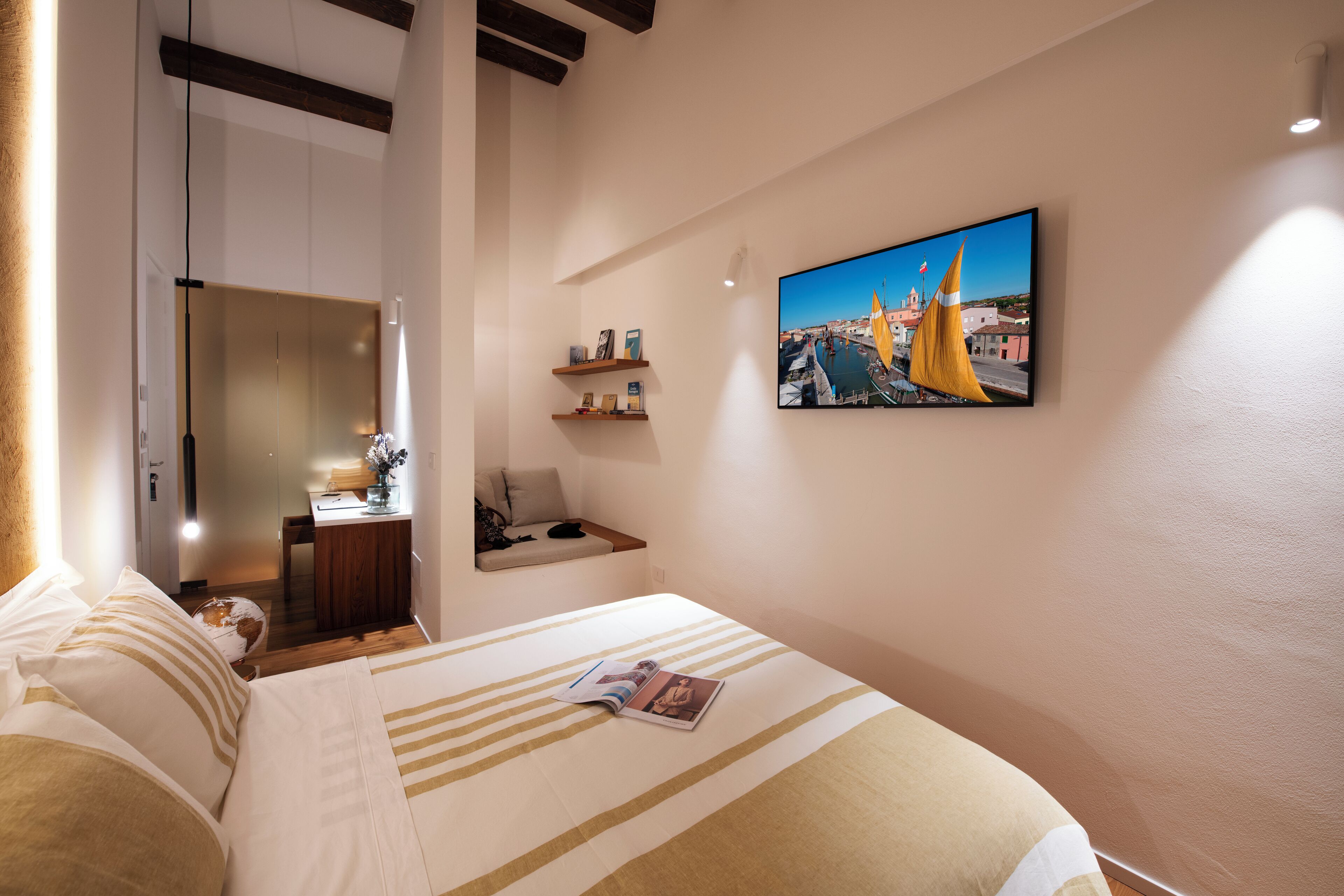 Quarto com cama, televisão na parede, pequena escrivaninha com cadeira e janela com vista para a cidade.