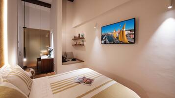 Quarto com cama, televisão na parede, pequena escrivaninha com cadeira e janela com vista para a cidade.