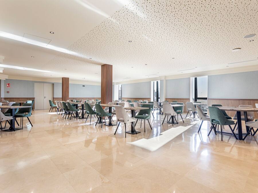 Uma sala de conferências ampla, com várias mesas e cadeiras, piso lustroso e teto com padrão único.