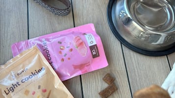 Uma mesa de madeira com duas embalagens de ração para cães, um comedouro e uma coleira.