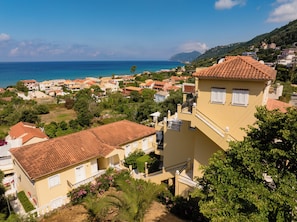 Uma cidade costeira com edifícios de telhados em terracota, um edifício amarelo proeminente com varanda, e vista para o mar.