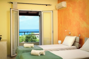 Quarto de hotel com duas camas, uma varanda e vista para o mar, e um ar condicionado.