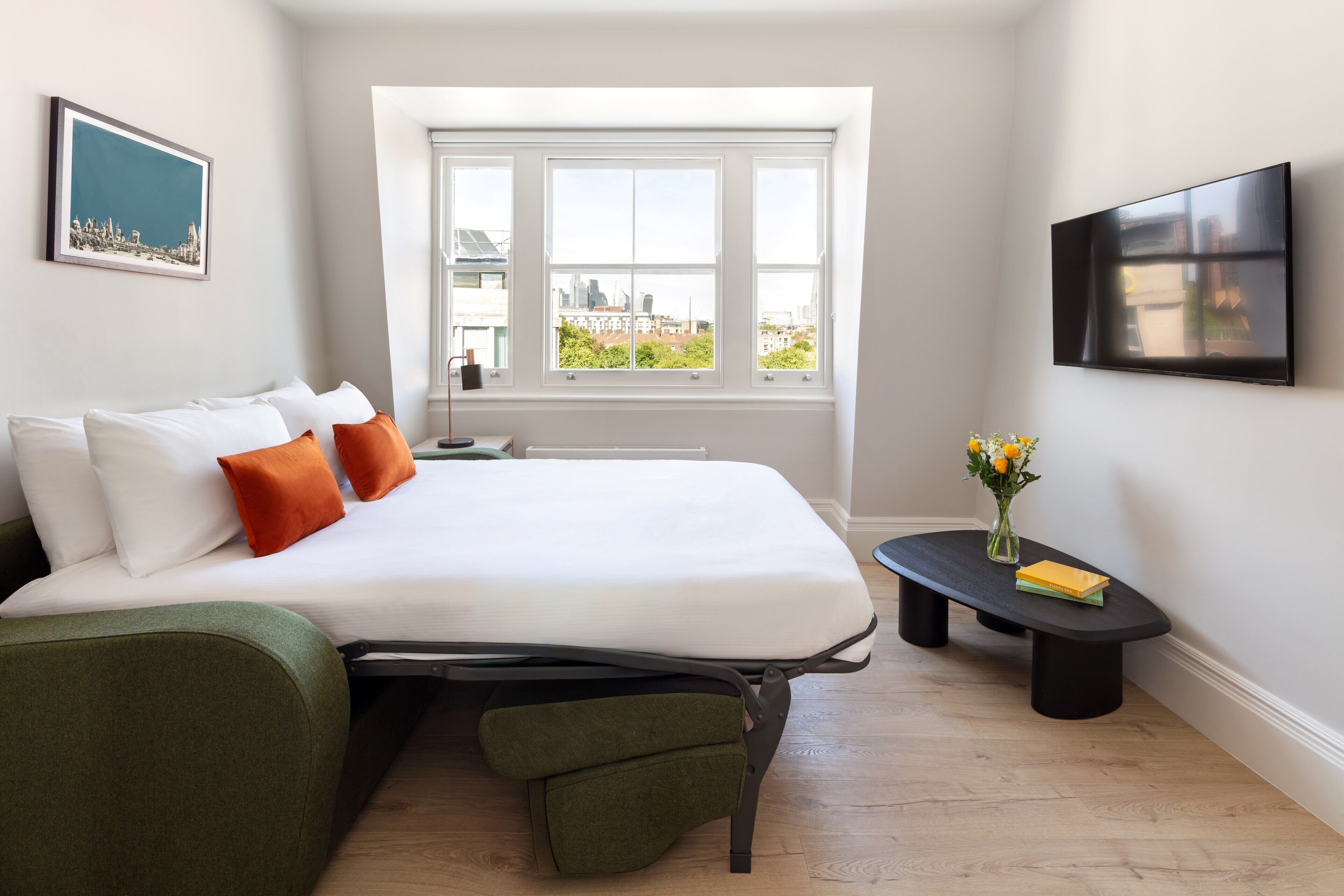 Quarto moderno com cama, mesa de cabeceira, janela com vista para a cidade e televisão de tela plana na parede.