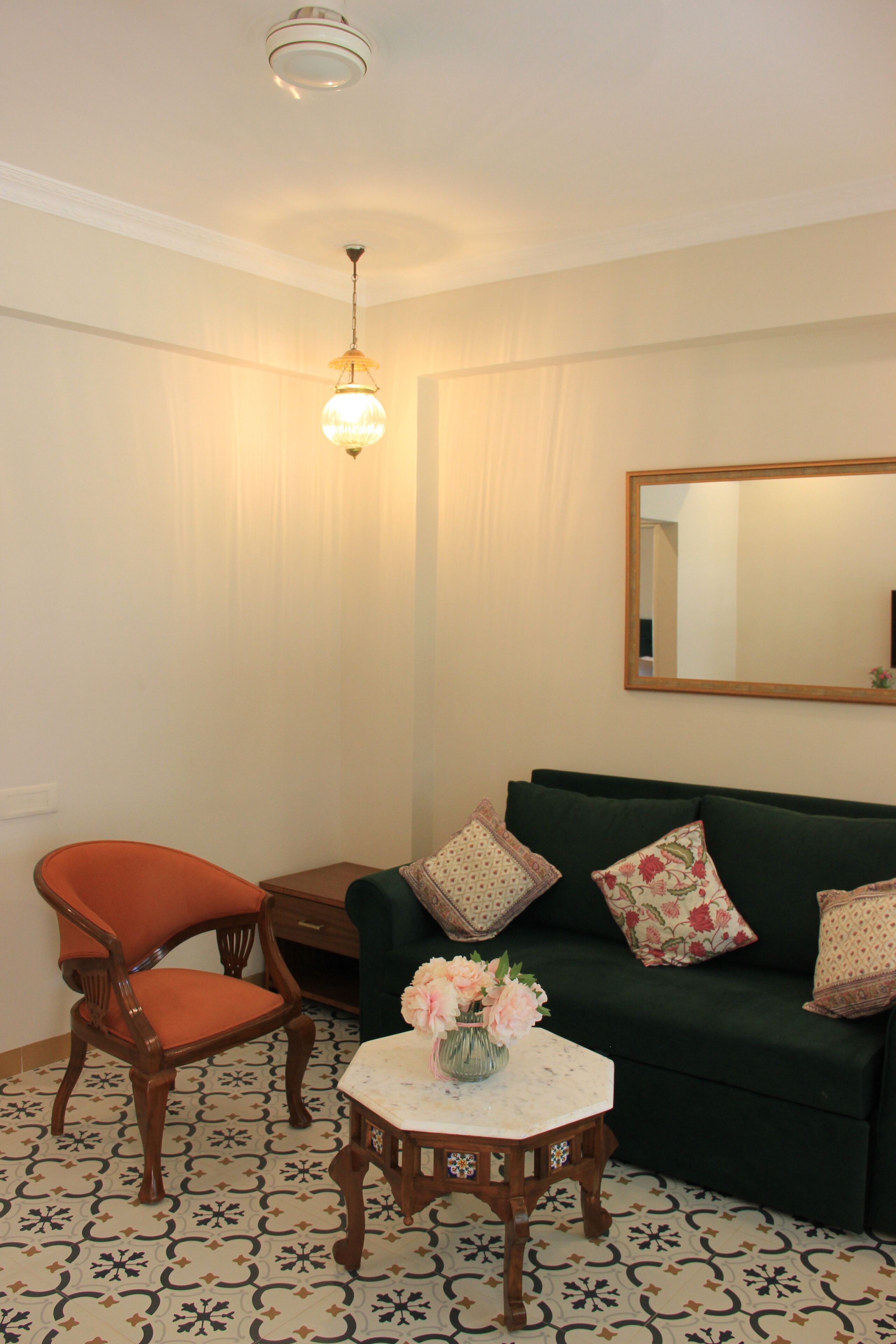 Uma sala de estar com um sofá verde, uma poltrona laranja e uma pequena mesa com um vaso de flores.