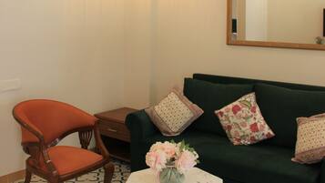 Uma sala de estar com um sofá verde, uma poltrona laranja e uma pequena mesa com um vaso de flores.