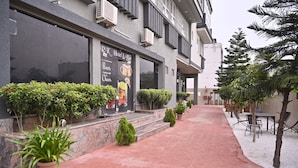 Exterior de hotel com caminho vermelho, plantas em vasos e área de estar ao ar livre.
