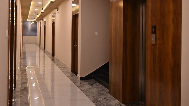 Um corredor comprido e bem iluminado, com painéis de madeira em uma lateral e piso de mármore.