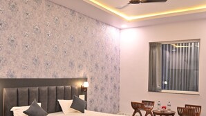 Quarto moderno com cama, ventilador de teto, pequena mesa com cadeiras e janela com cortinas.