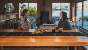 Uma sala de jantar com mesa de madeira, duas pessoas sentadas, vista para o exterior e lareira.